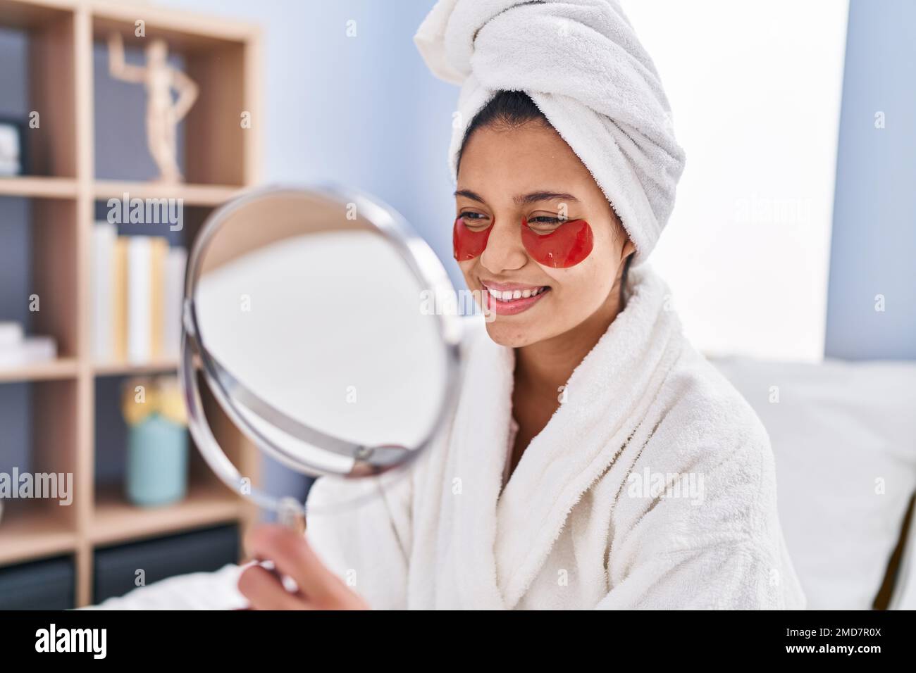 Young latin woman having baggy eyes treatment looking on mirror at ...