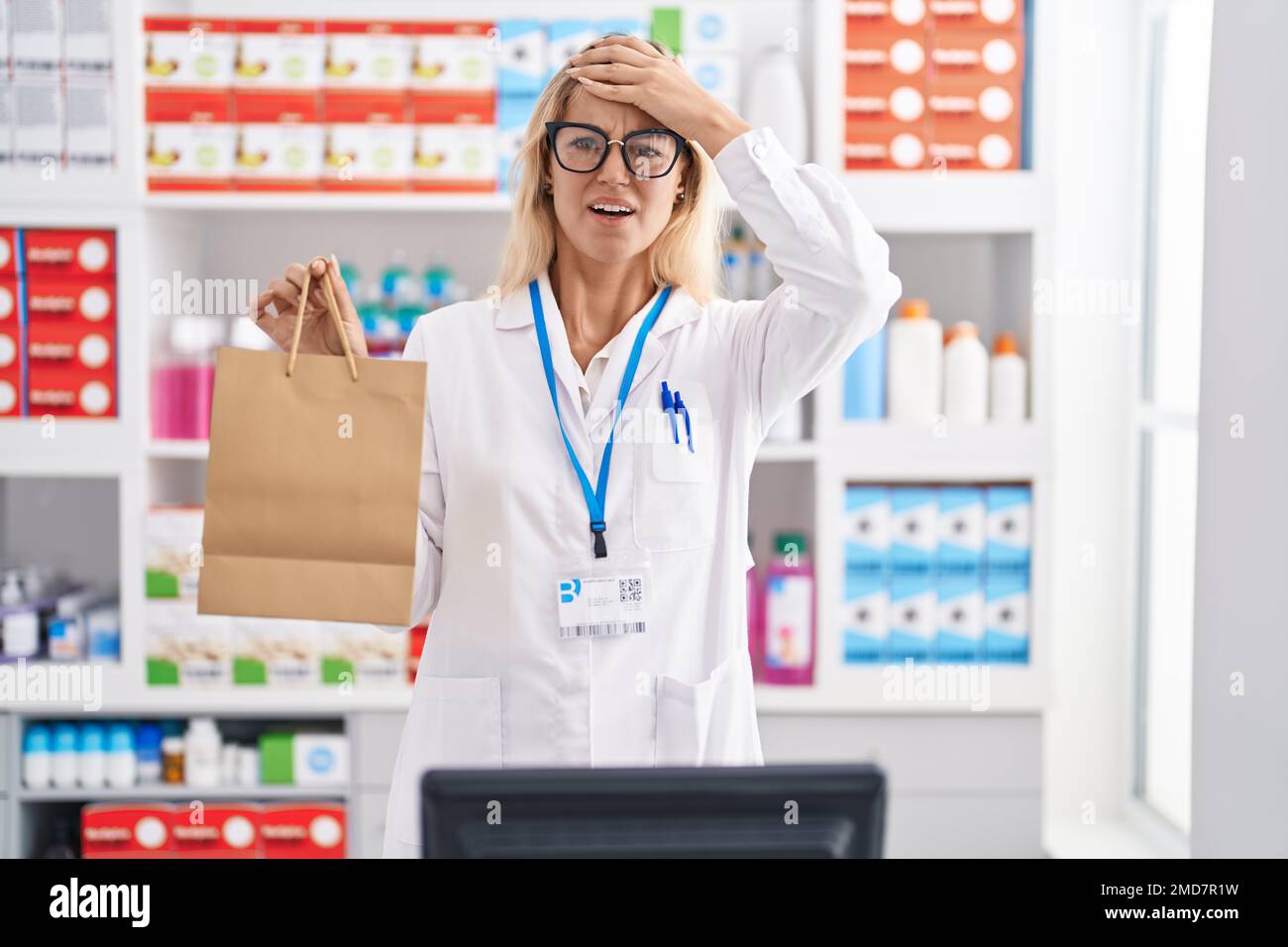 Young blonde woman working at pharmacy drugstore holding paper bag ...