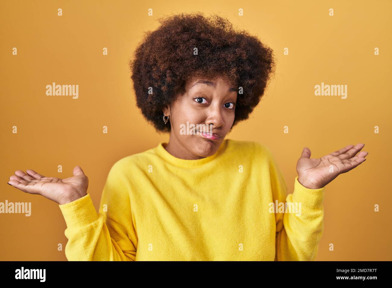 Young african american woman standing over yellow background clueless ...