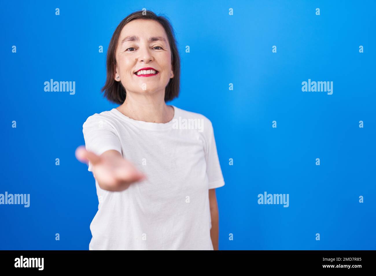 Middle age hispanic woman standing over blue background smiling ...