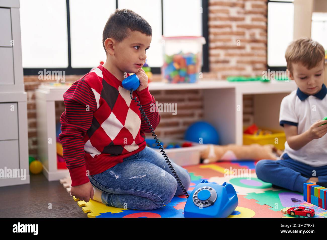 Two kids playing with telephone toy sitting on floor at kindergarten ...