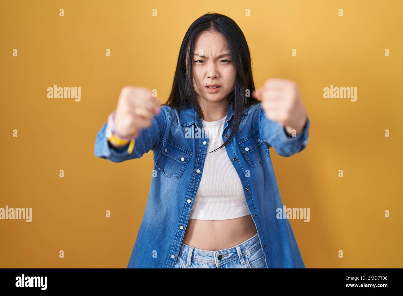 Young asian woman standing over yellow background angry and mad raising ...
