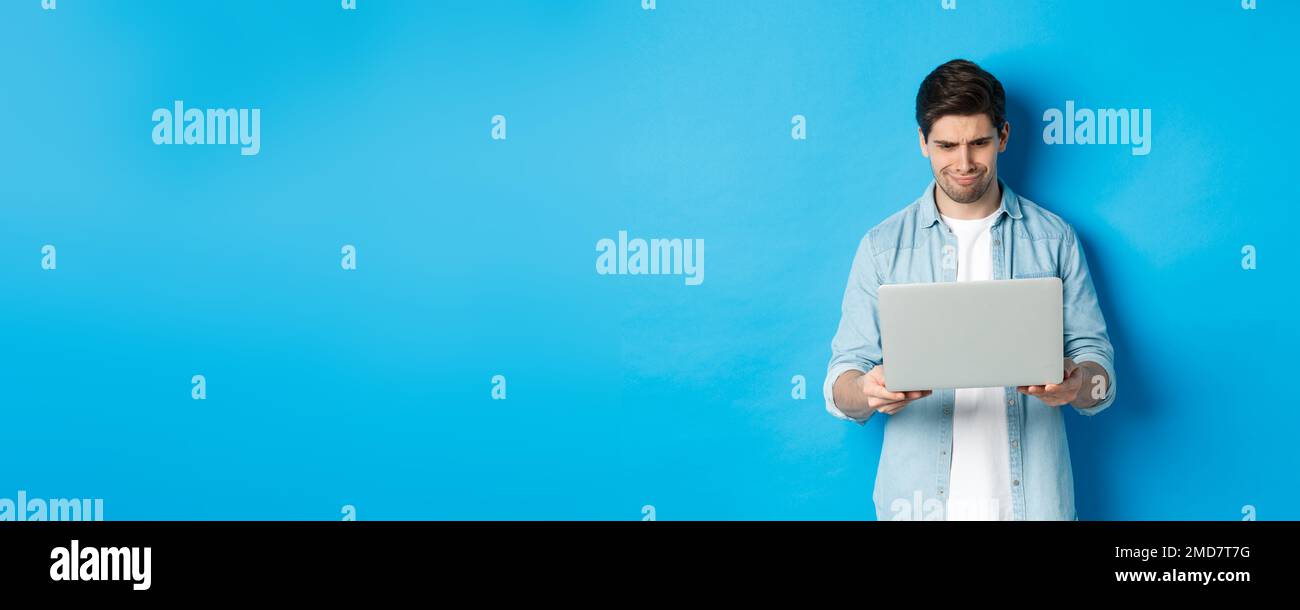 Disappointed handsome man looking at laptop screen and grimacing ...