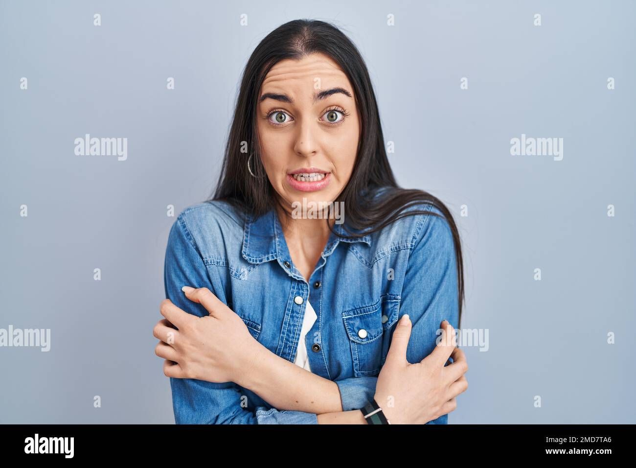 Hispanic woman standing over blue background shaking and freezing for ...