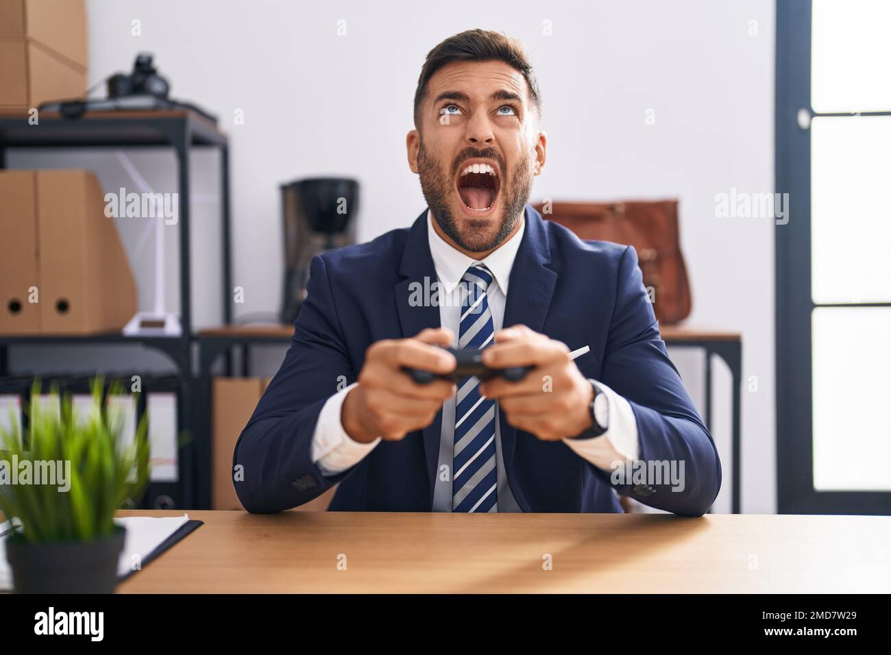 Handsome hispanic man playing video games at the office angry and mad ...