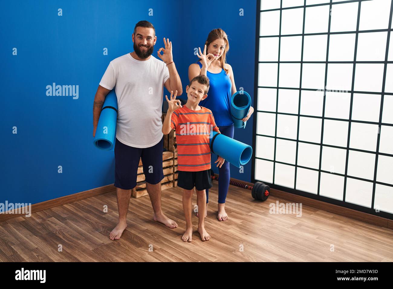 Family of three holding yoga mat doing ok sign with fingers, smiling ...