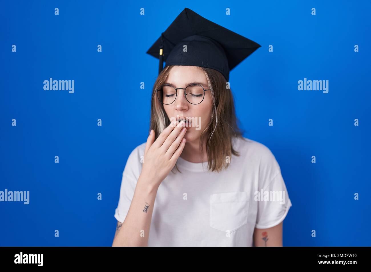 Blonde caucasian woman wearing graduation cap bored yawning tired ...