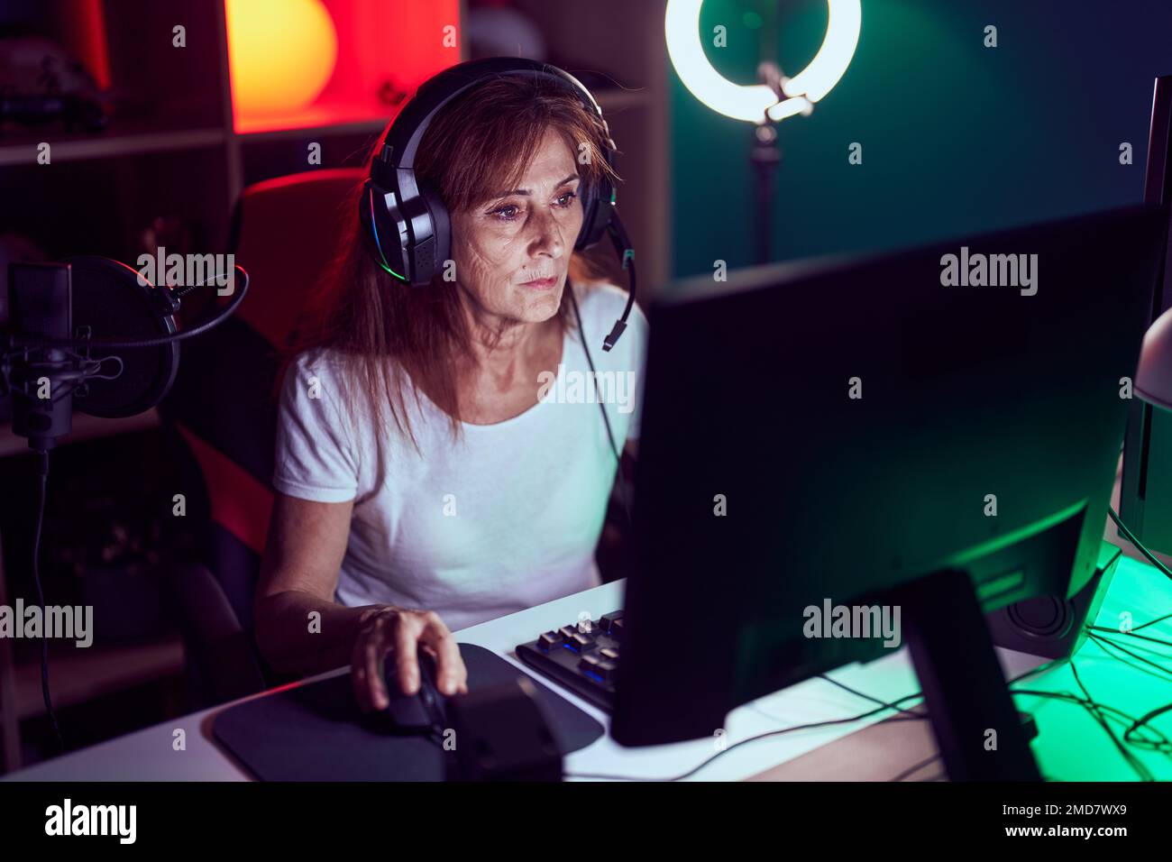 Middle age woman streamer playing video game using computer at gaming ...