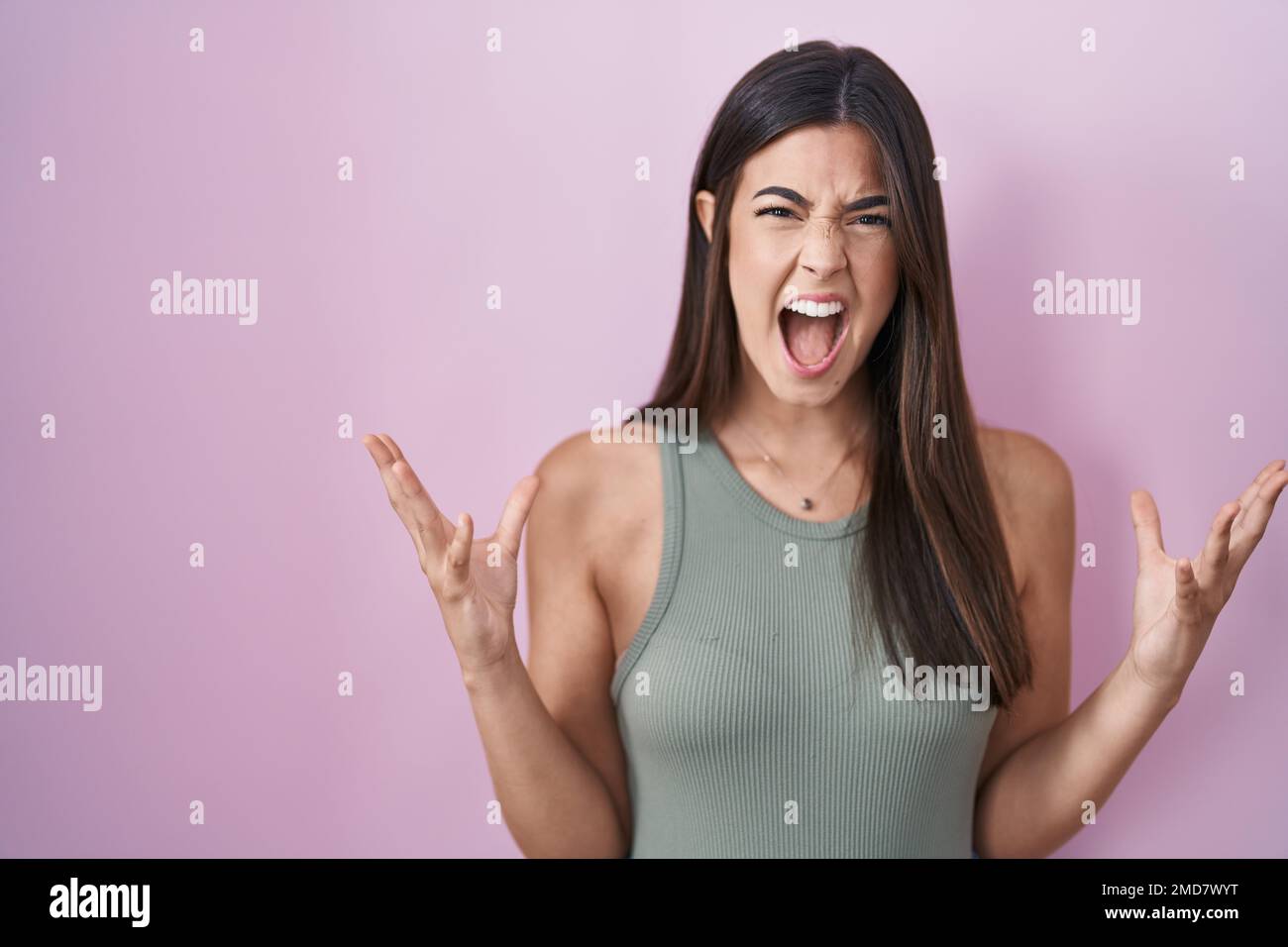 Hispanic woman standing over pink background crazy and mad shouting and ...