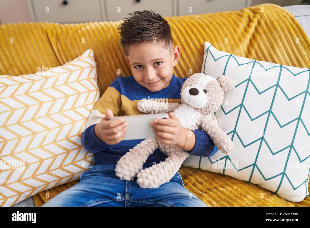Adorable hispanic boy hugging teddy bear watching video on smartphone ...