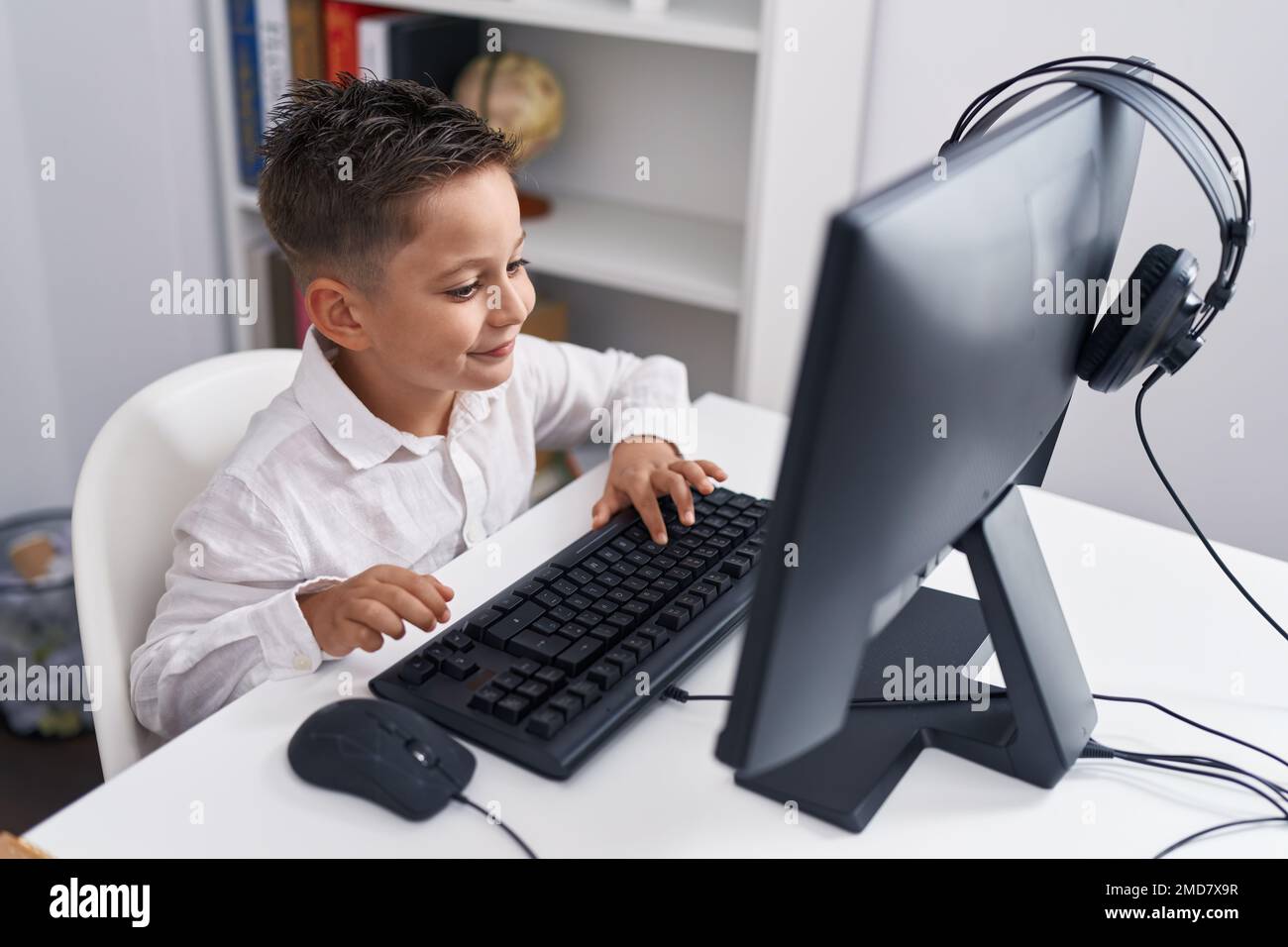 Adorable hispanic boy student using computer sitting on table at ...