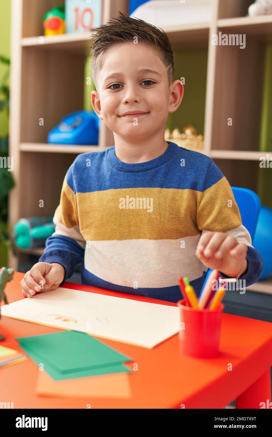 Adorable hispanic boy preschool student sitting on table drawing on ...