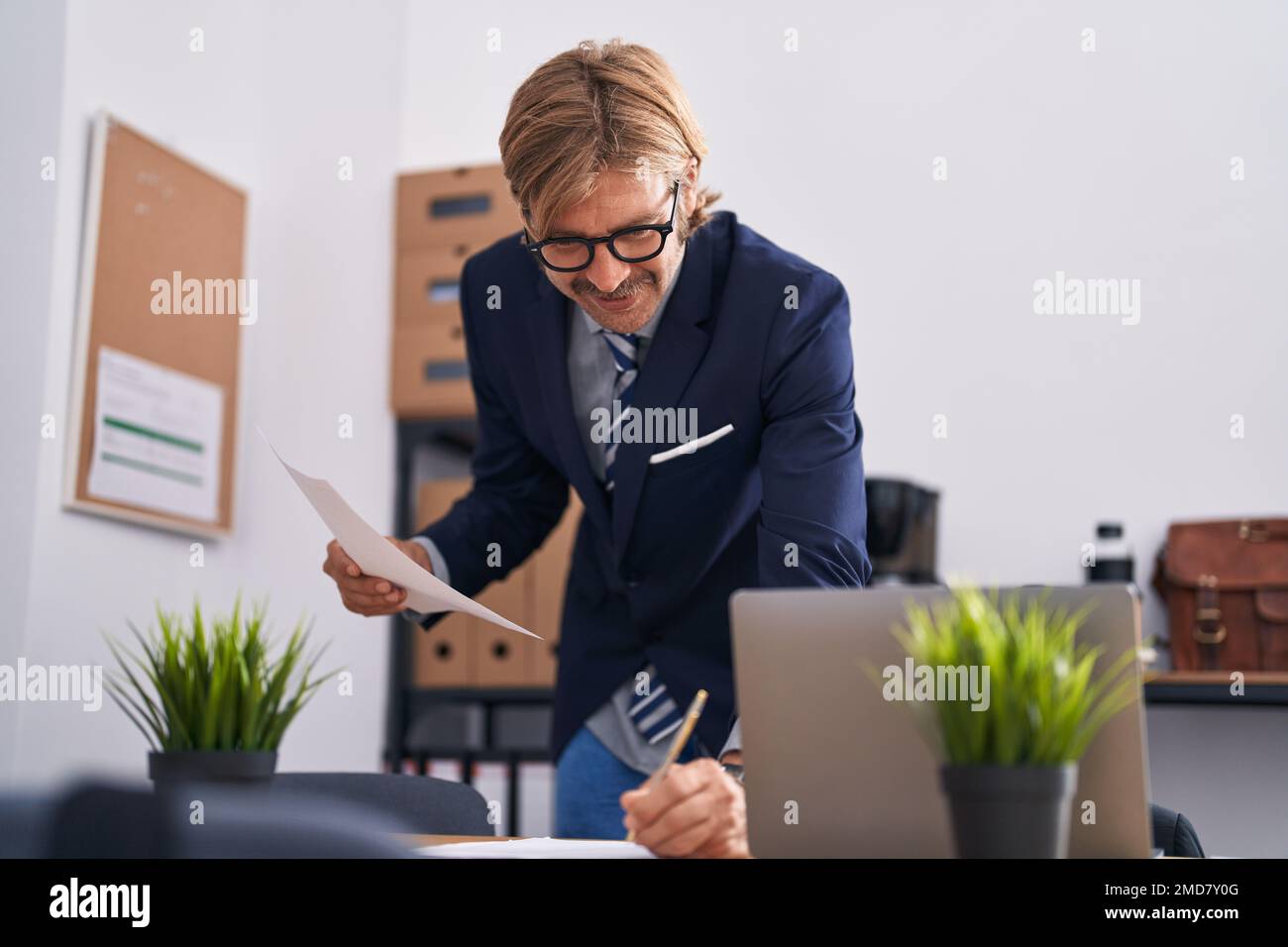 Young blond man business worker using laptop writing on document at ...