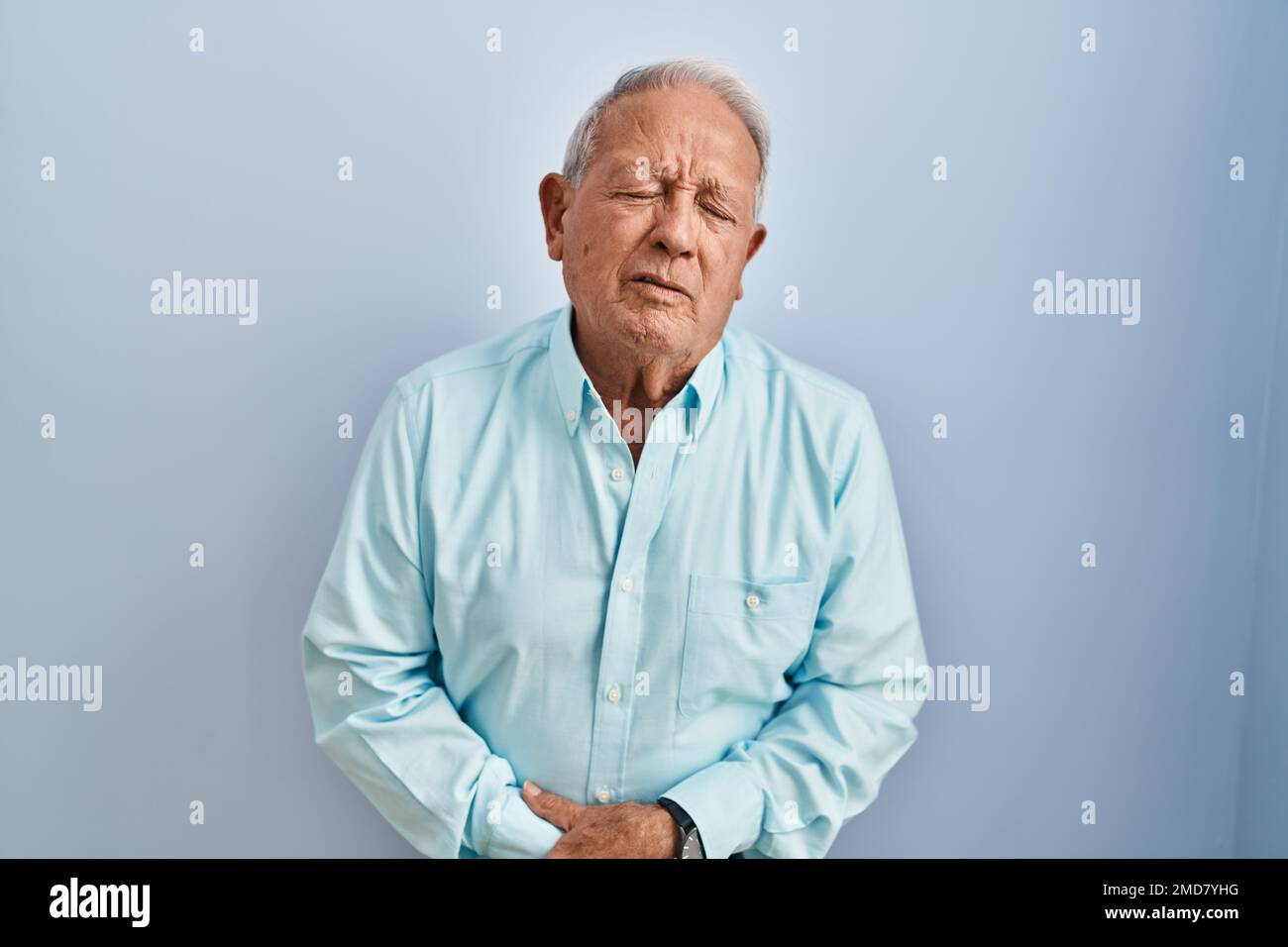 Senior man with grey hair standing over blue background with hand on ...