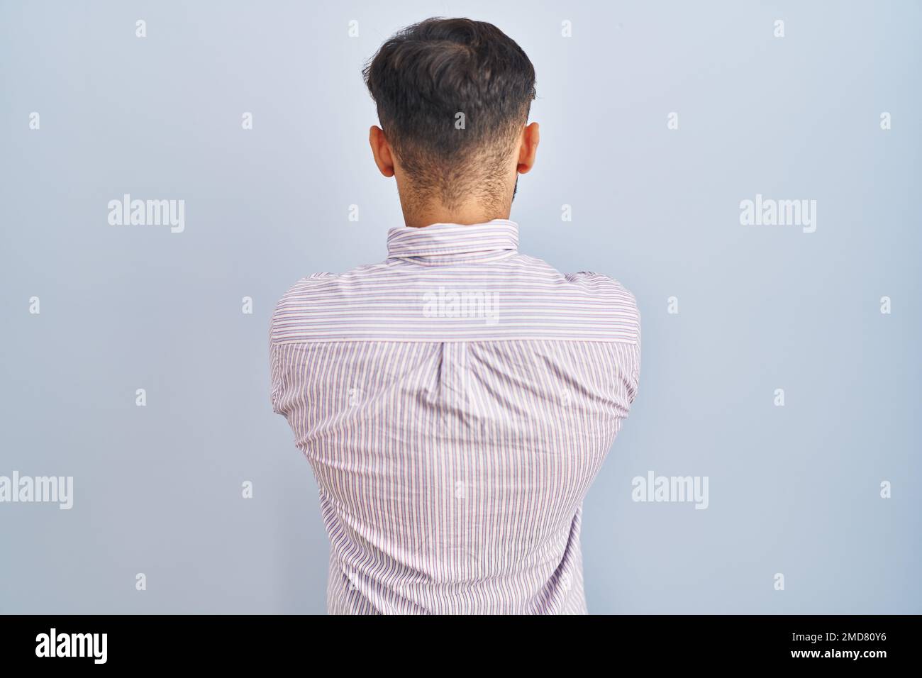 Arab man with beard standing over blue background standing backwards ...
