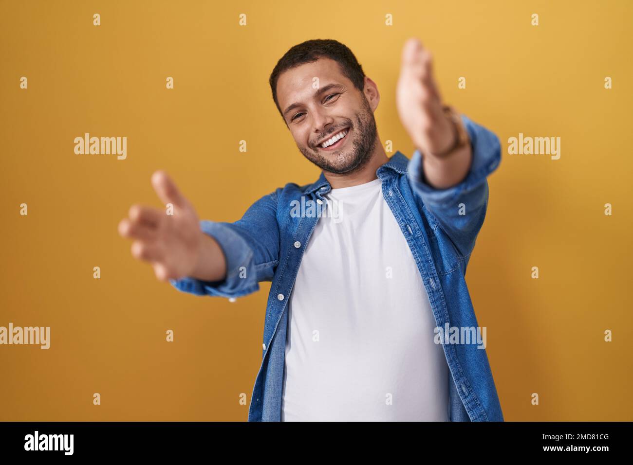 Hispanic man standing over yellow background looking at the camera ...