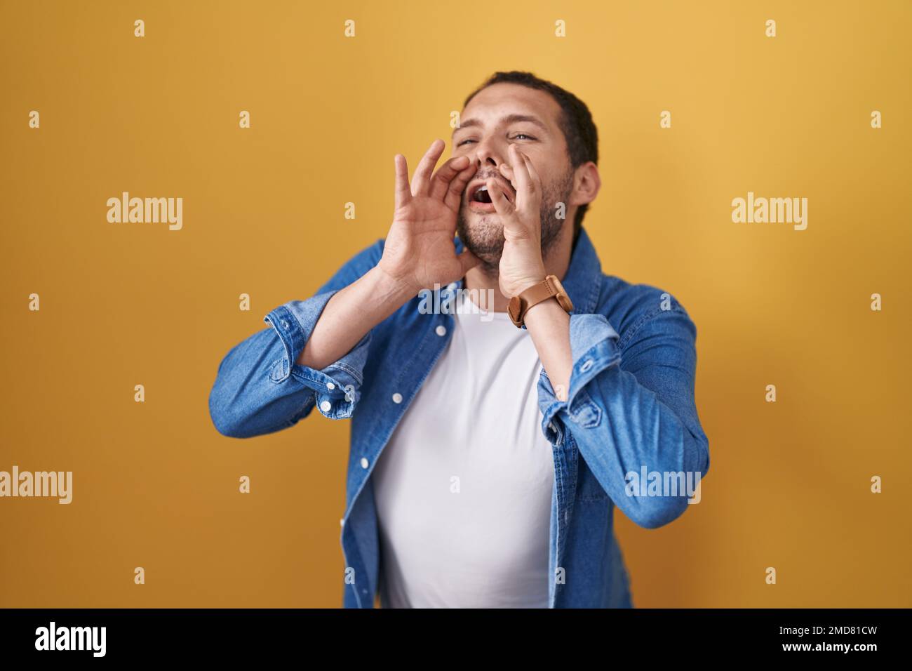 Hispanic man standing over yellow background shouting angry out loud ...
