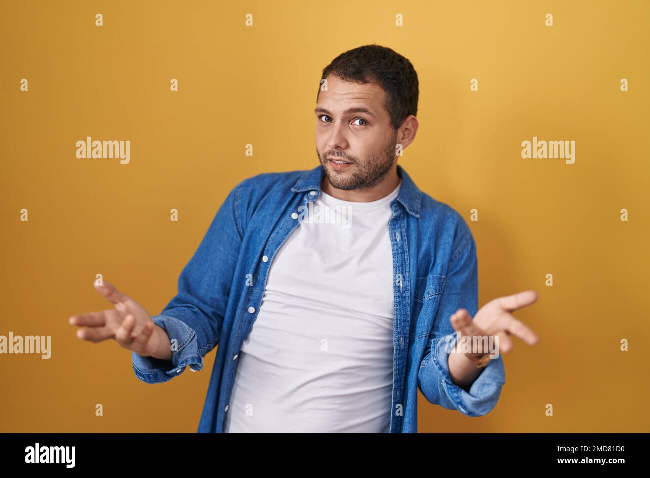 Hispanic man standing over yellow background clueless and confused with ...