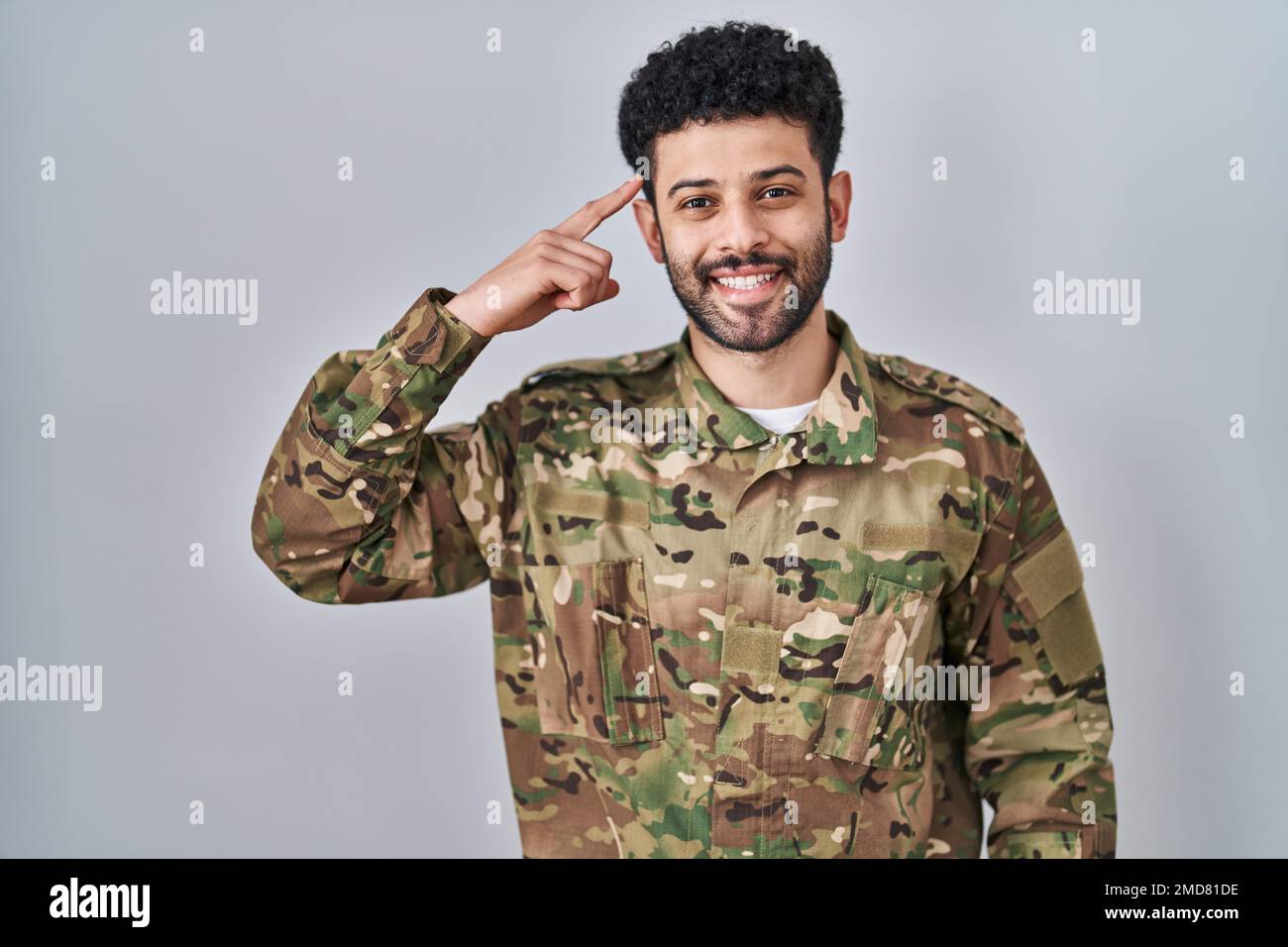 Arab man wearing camouflage army uniform smiling pointing to head with ...