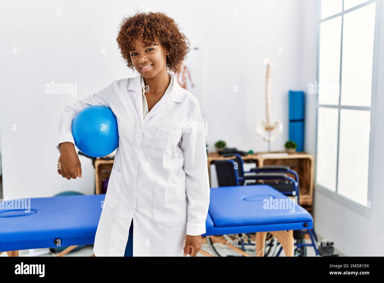 Young african american woman wearing physio uniform holding fit ball at ...