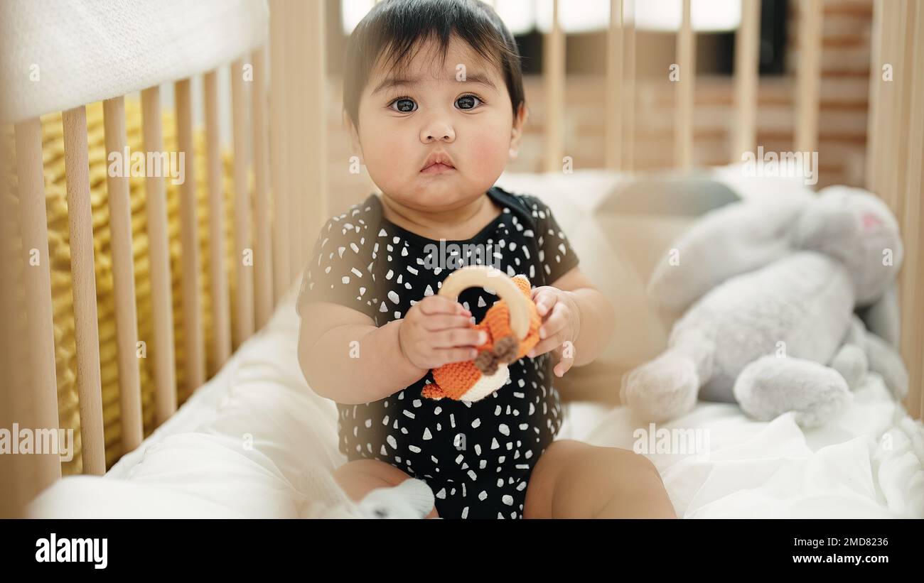 Adorable hispanic baby holding toy sitting on cradle at bedroom Stock ...