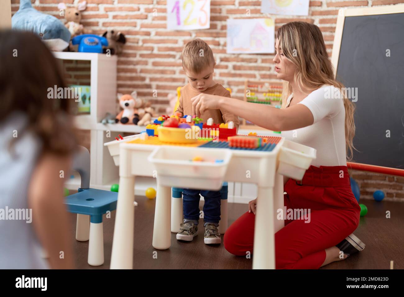 Teacher and toddler playing with construction blocks sitting on table ...