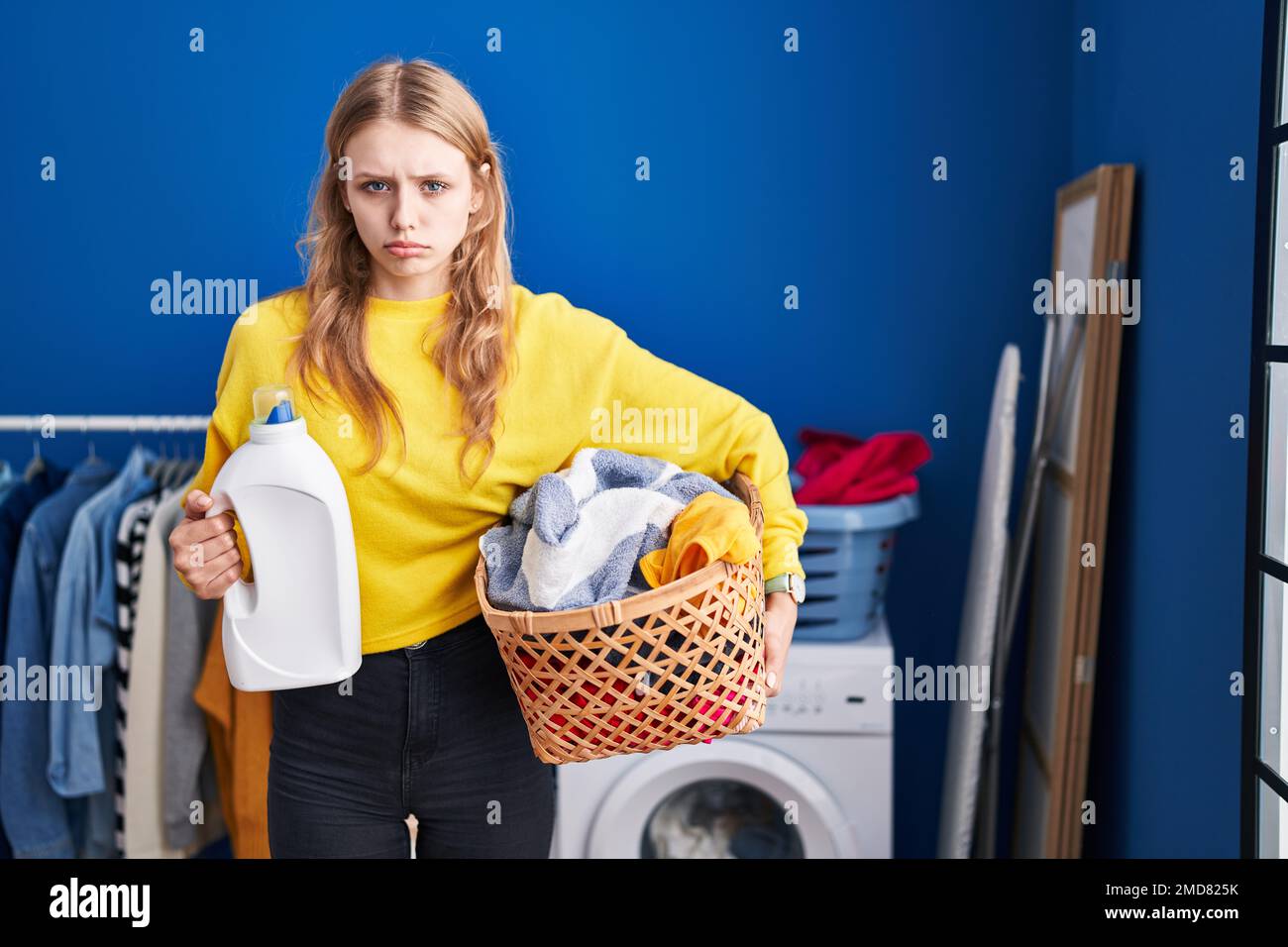 Young caucasian woman holding laundry basket and detergent bottle depressed and worry for ...