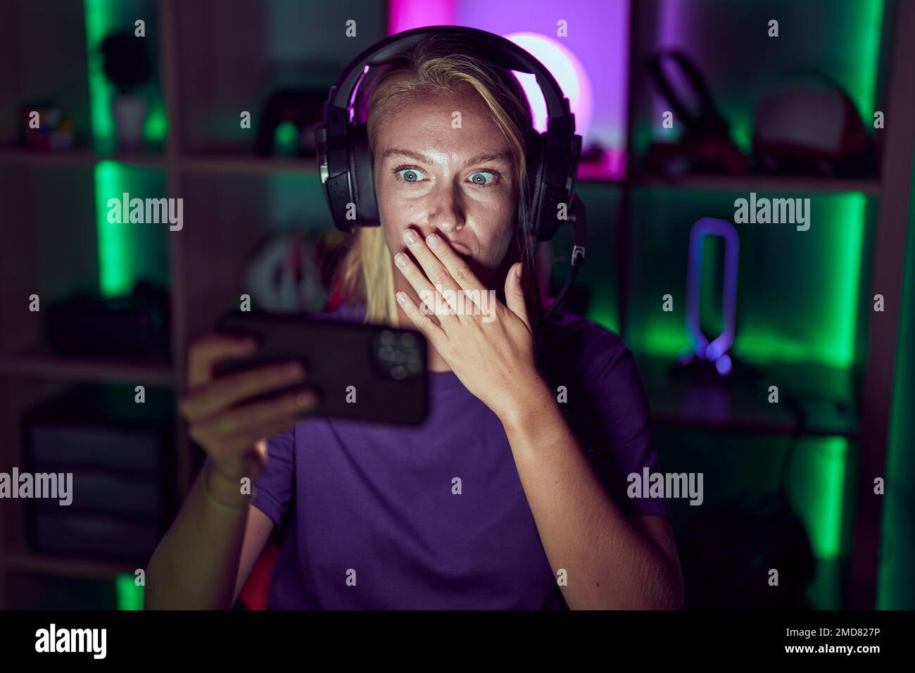 Young gamer woman playing video games with smartphone covering mouth ...