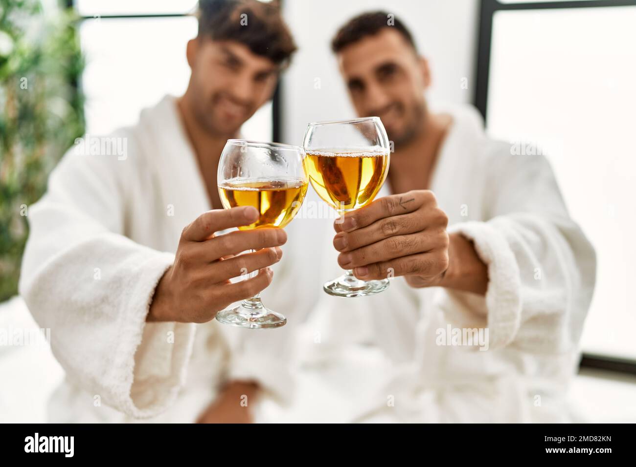 Two hispanic men couple toasting with champagne sitting on massage ...