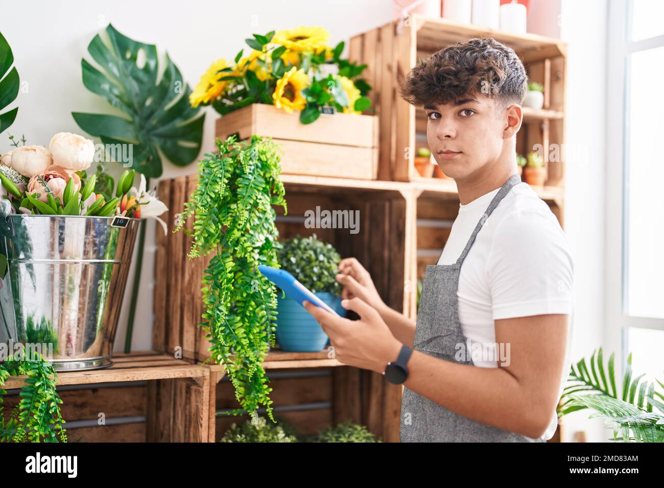 Young hispanic teenager florist using touchpad touching plant at flower ...