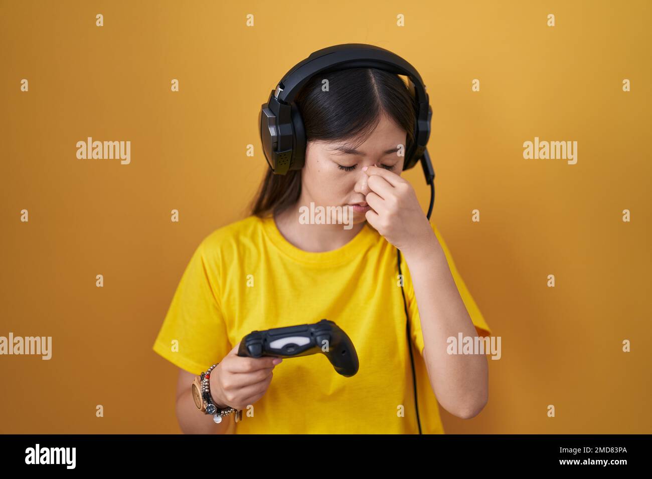 Chinese young woman playing video game holding controller tired rubbing ...