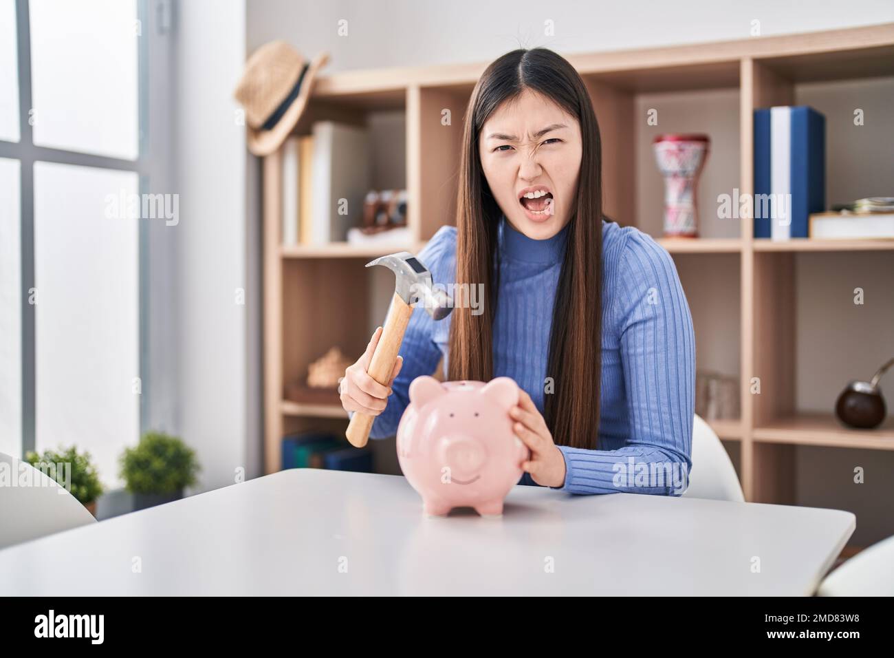 Chinese young woman holding hammer and piggy bank angry and mad ...