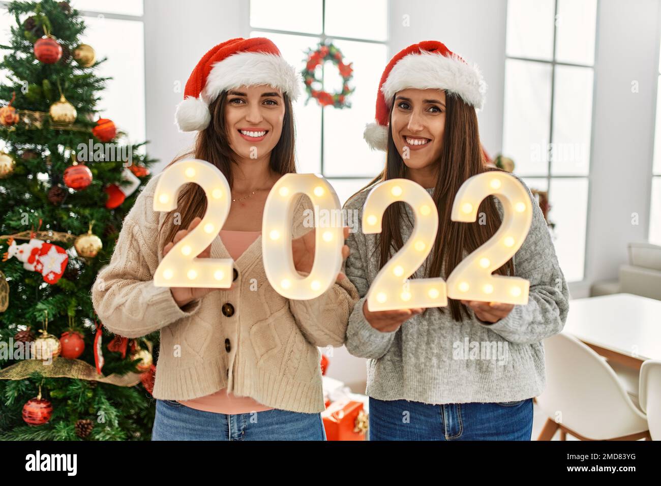 Two women celebrate new year holding 2022 lights standing by christmas ...