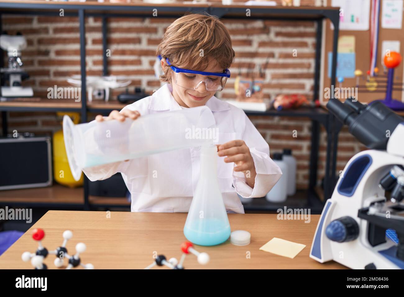 Adorable caucasian boy student pouring liquid on test tube at classroom ...