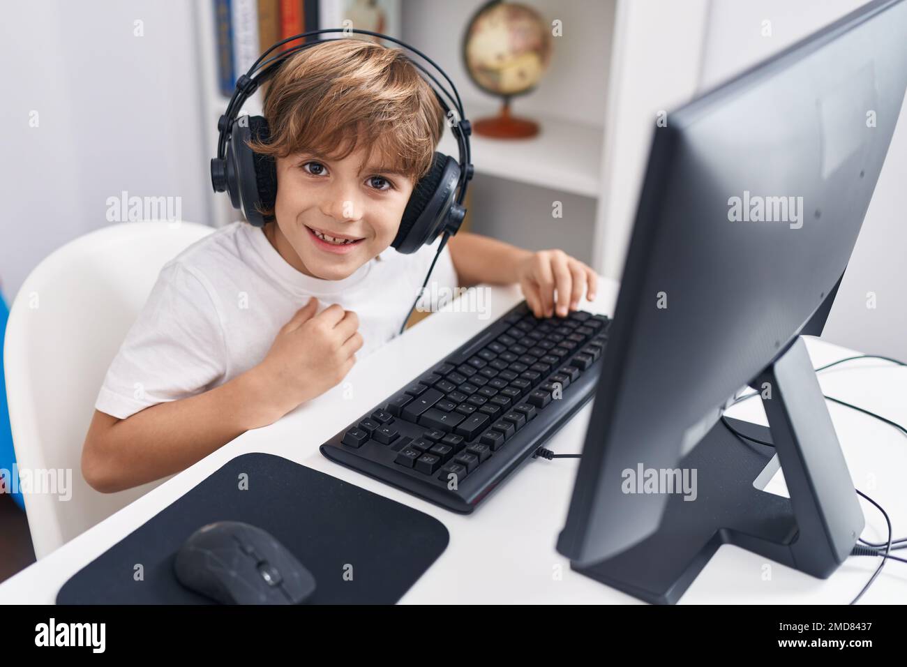 Adorable caucasian boy student using computer sitting on table at ...