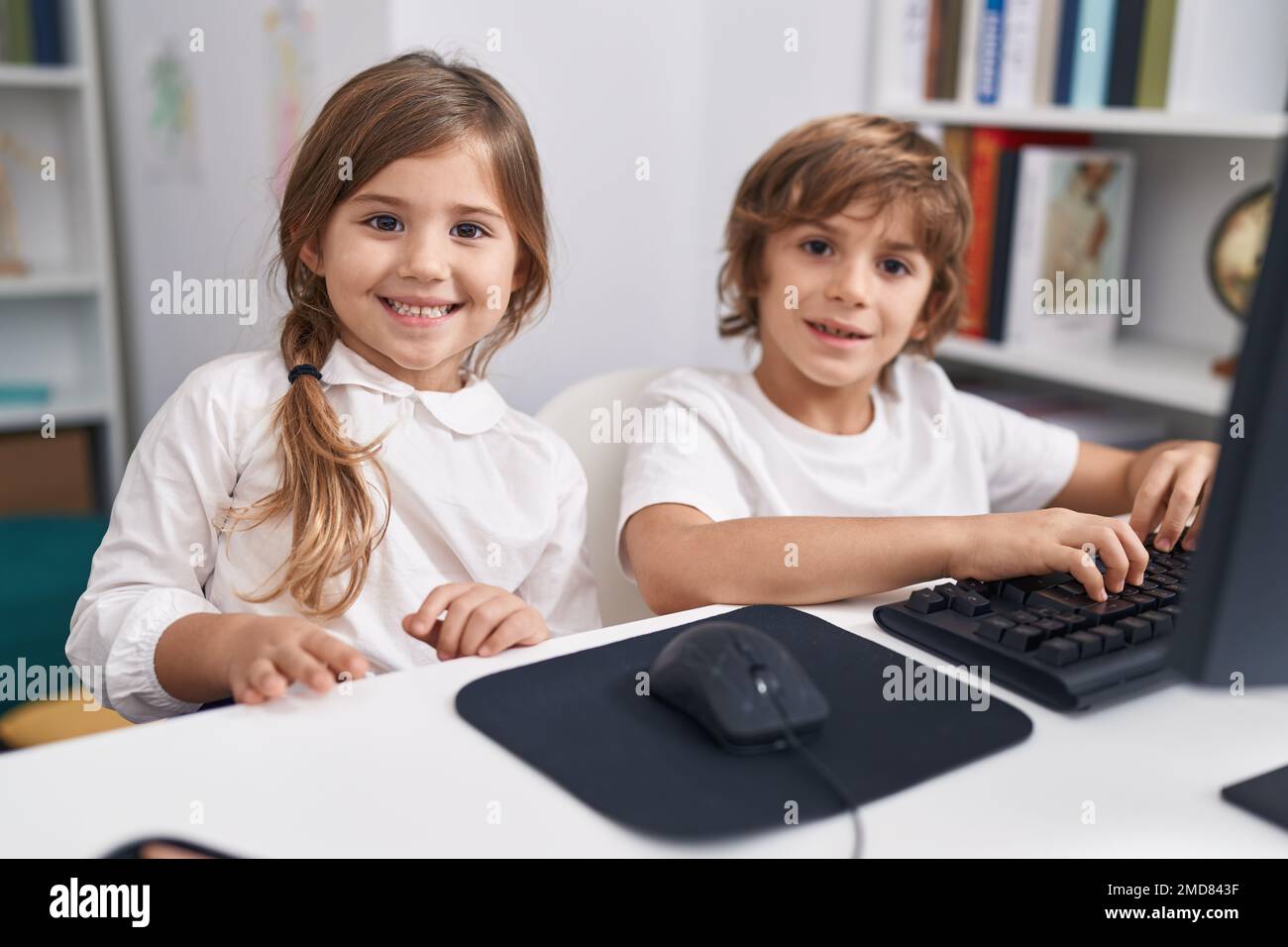 Brother and sister students using computer sitting on table at ...