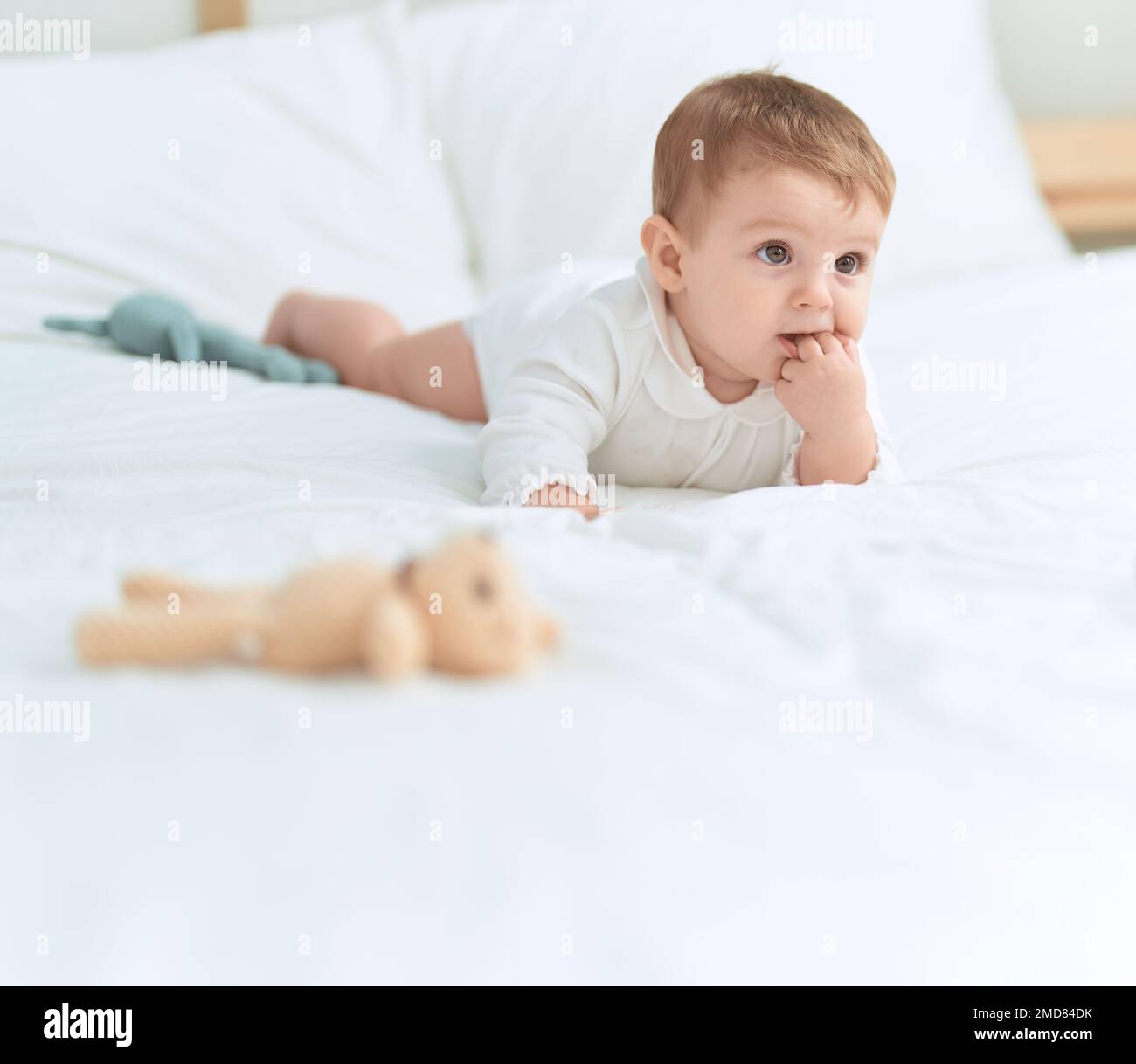 Adorable toddler lying on bed with teddy bear with serious expression ...