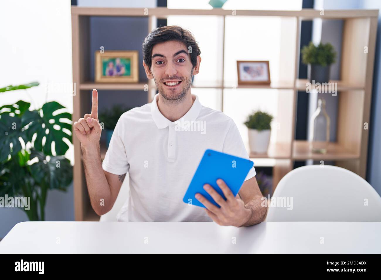 Young hispanic man using touchpad sitting on the table smiling with an ...