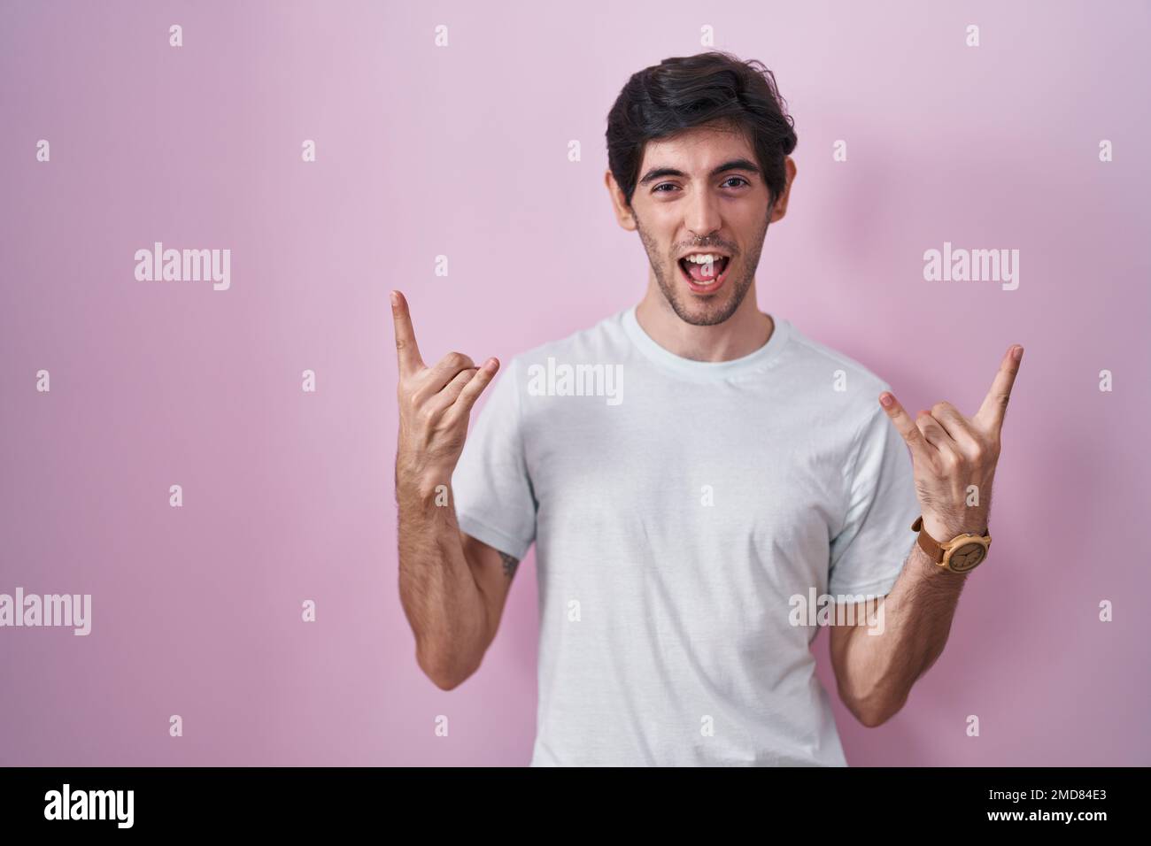 Young hispanic man standing over pink background shouting with crazy ...
