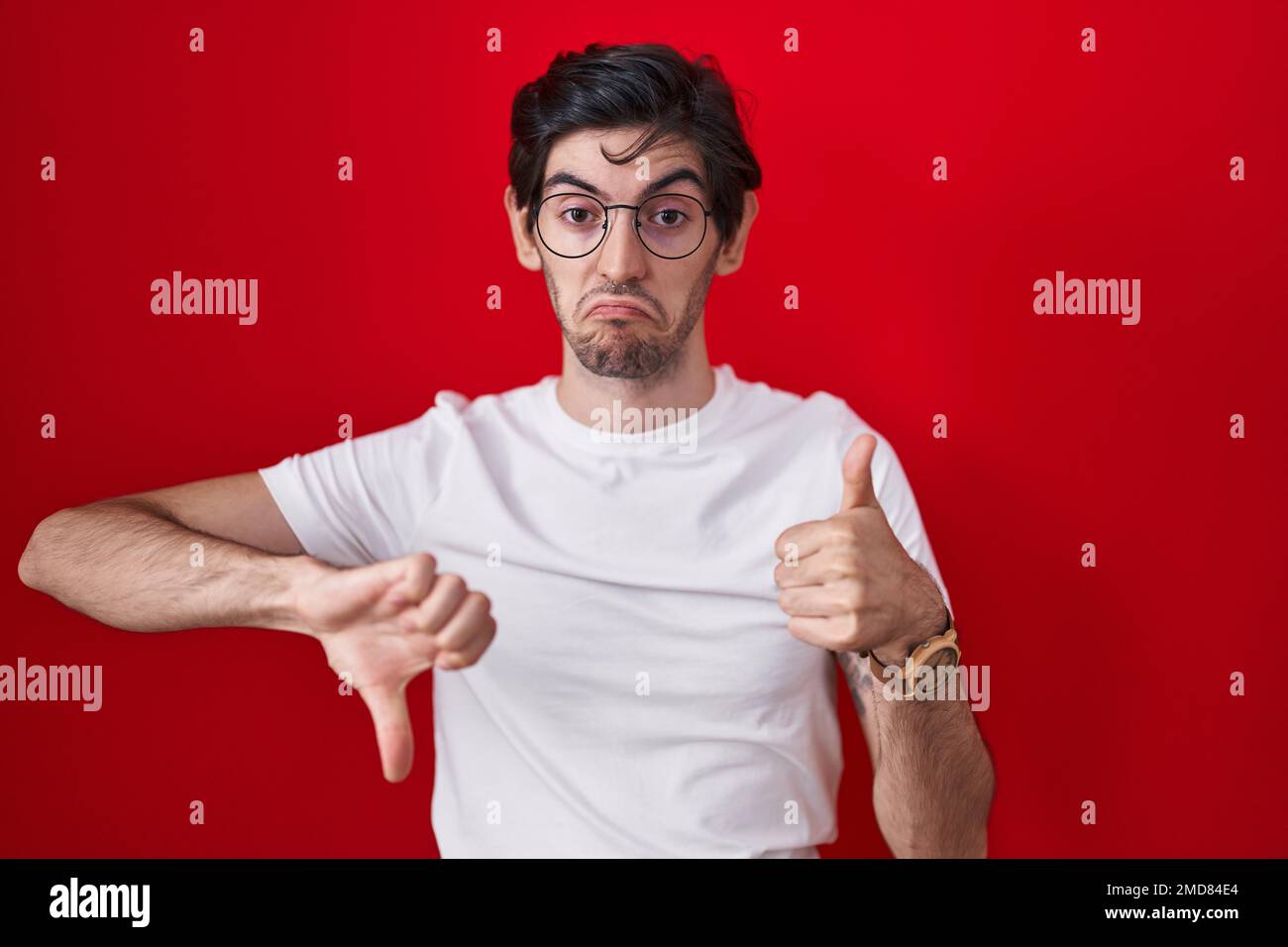 Young hispanic man standing over red background doing thumbs up and ...