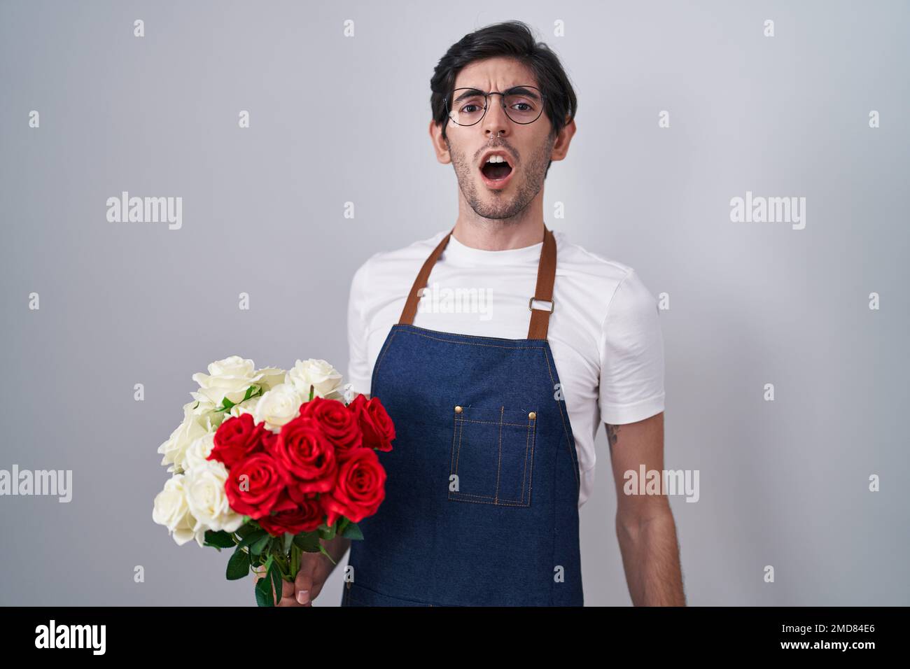 Young hispanic man holding bouquet of white and red roses angry and mad ...