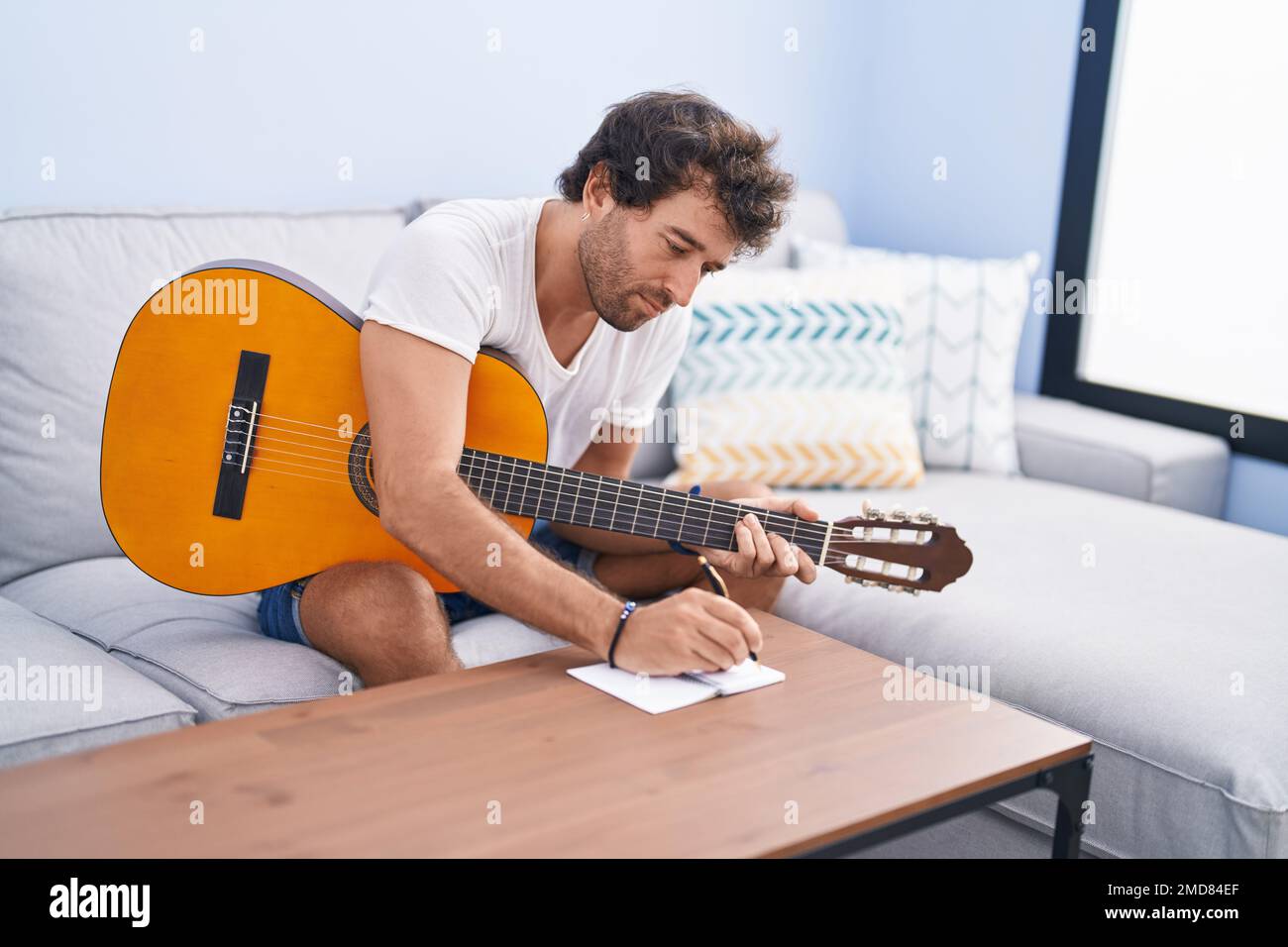 Young hispanic man playing classical guitar composing song at home ...