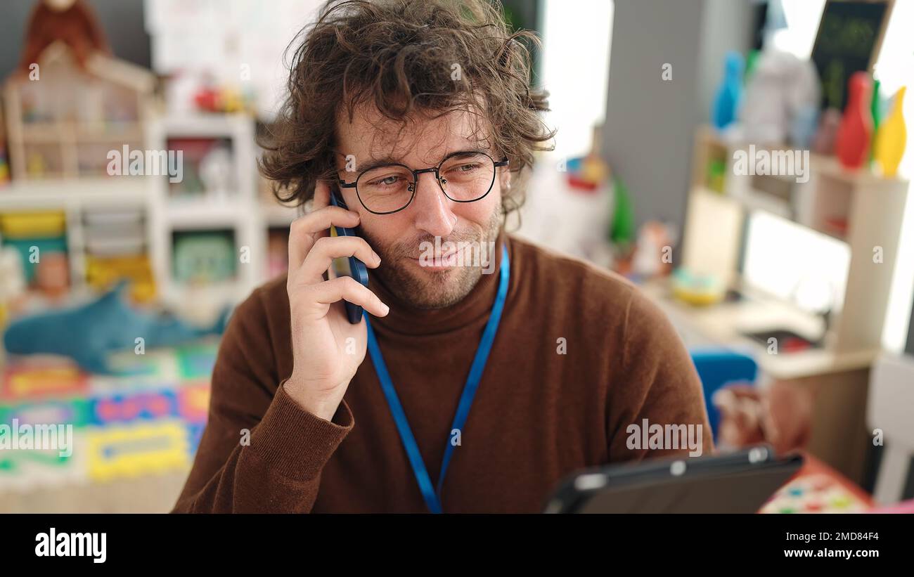 Young hispanic man preschool teacher using touchpad talking on ...