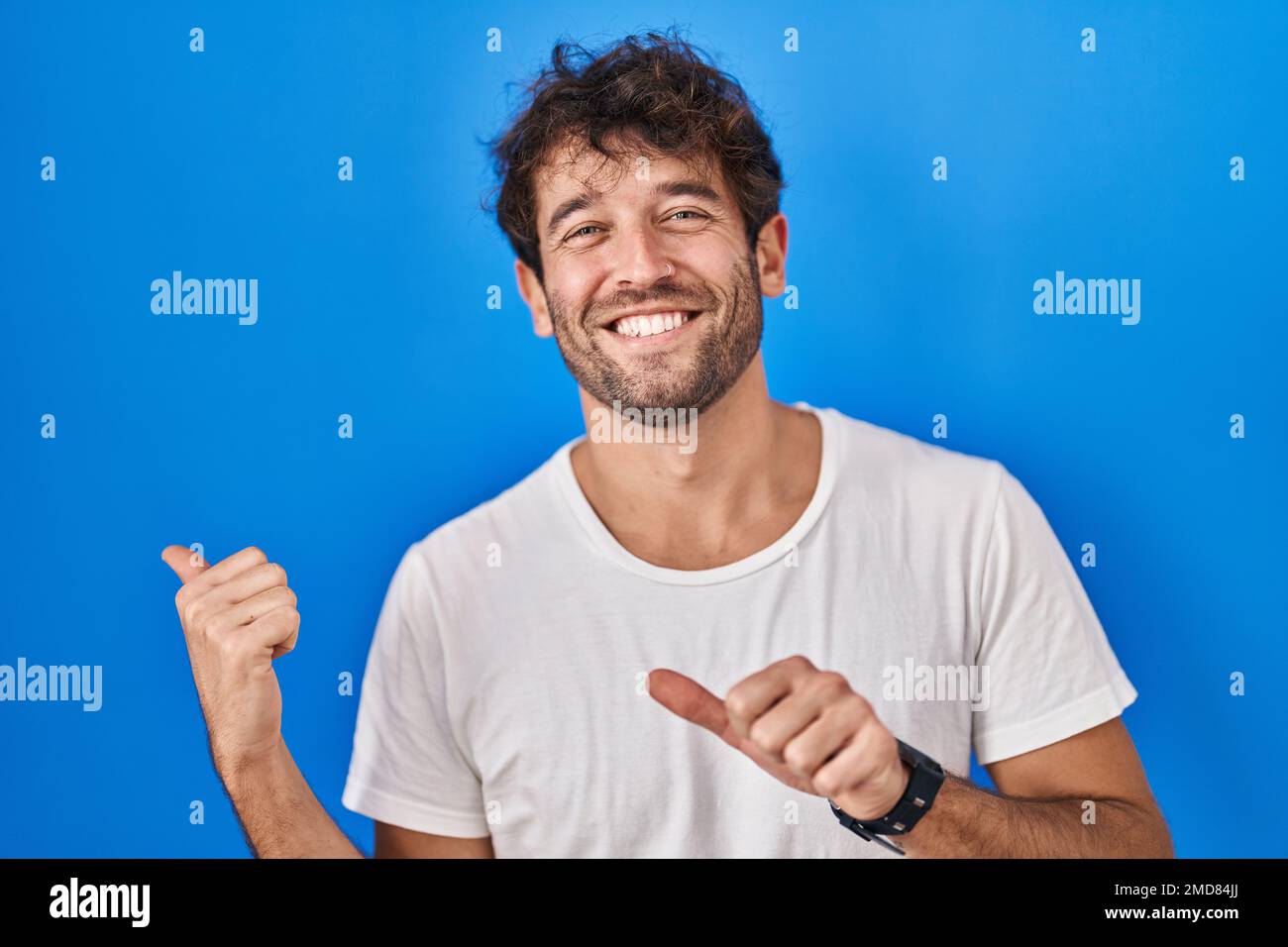 Hispanic young man standing over blue background pointing to the back ...
