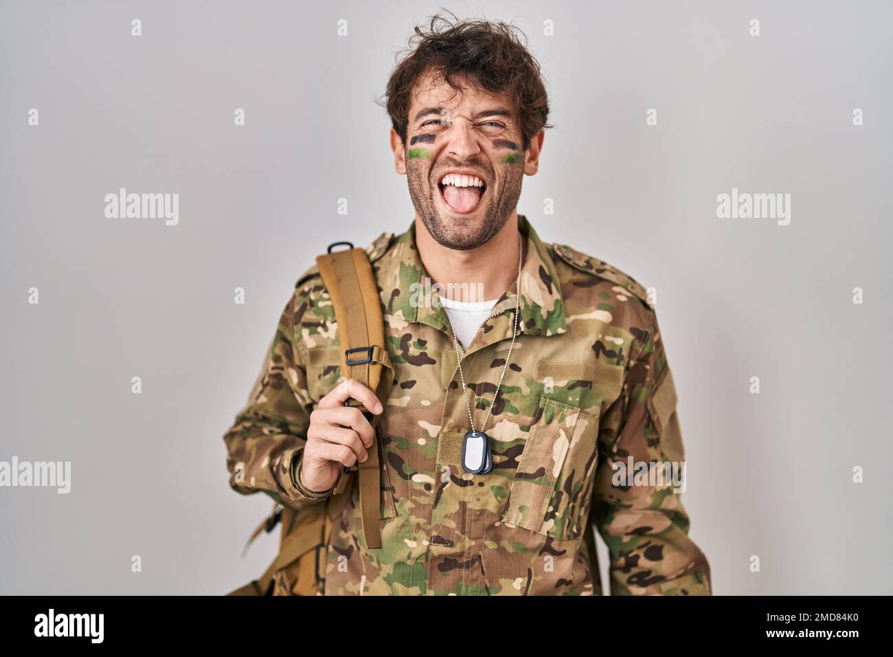 Hispanic young man wearing camouflage army uniform sticking tongue out ...