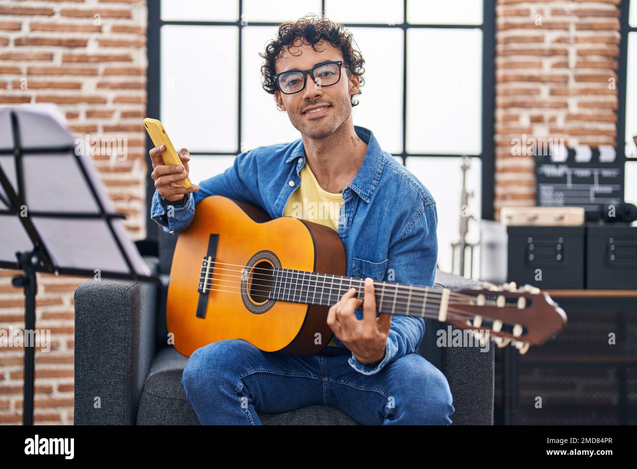 Young hispanic man musician playing classical guitar using smartphone ...