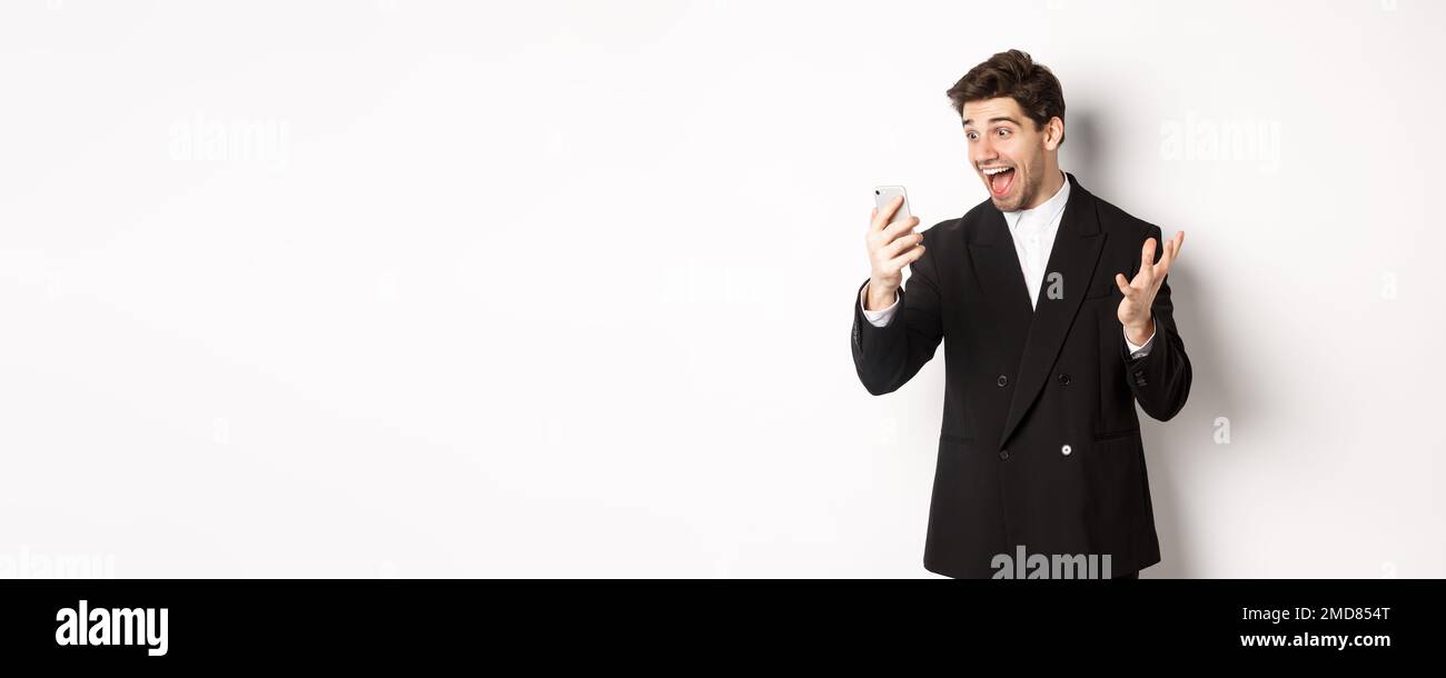 Portrait of happy smiling man in black suit, looking at smartphone ...