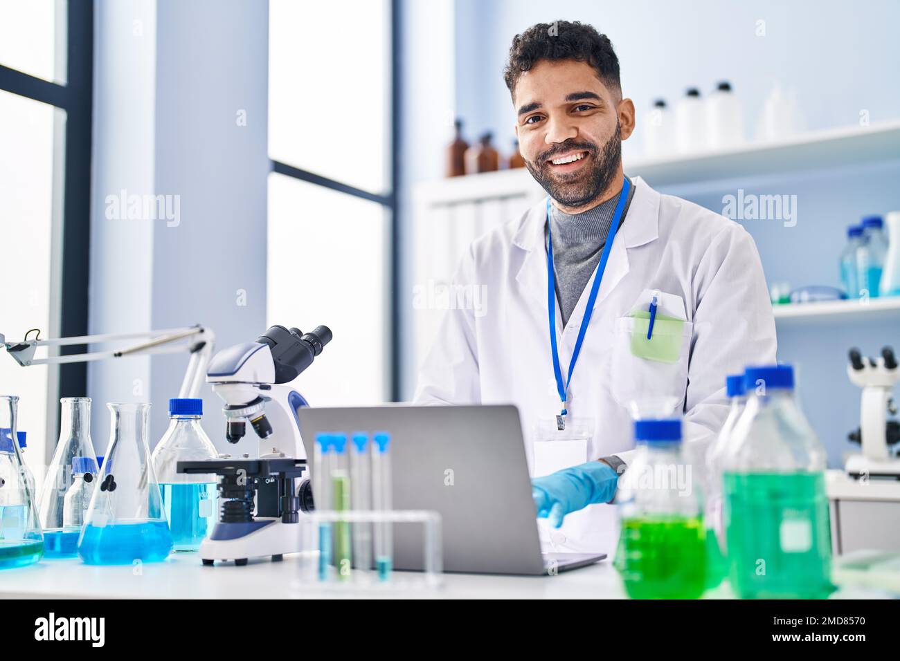 Young hispanic man wearing scientist uniform using laptop at laboratory ...