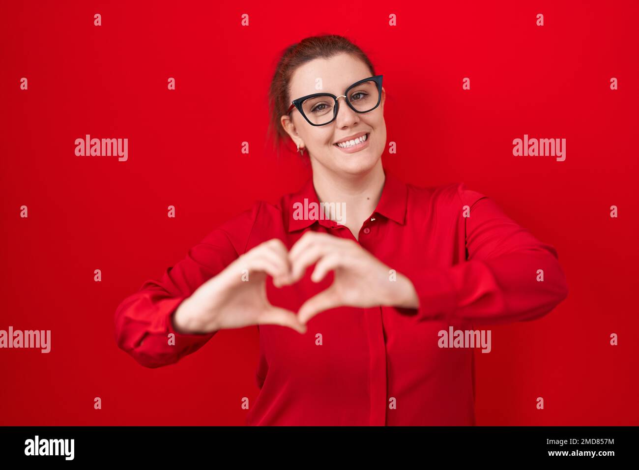 Young hispanic woman with red hair standing over red background smiling ...