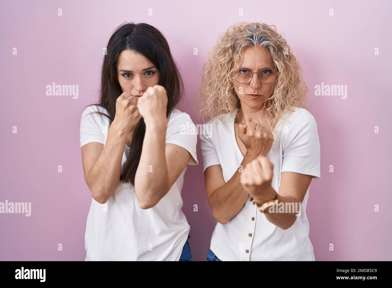 Mother and daughter standing together over pink background ready to ...